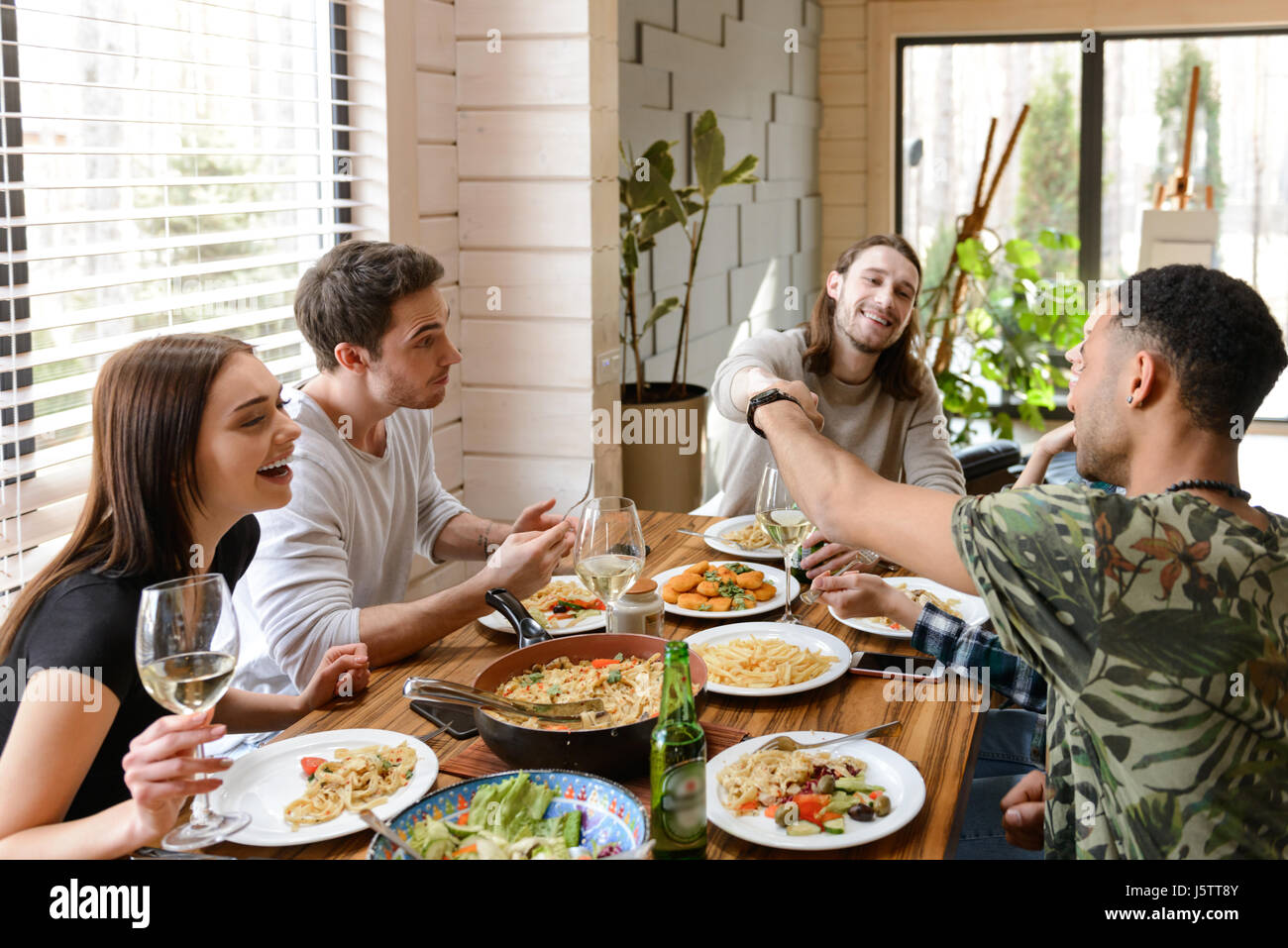 Group of cheerful young friends eating and having fun at the table at ...