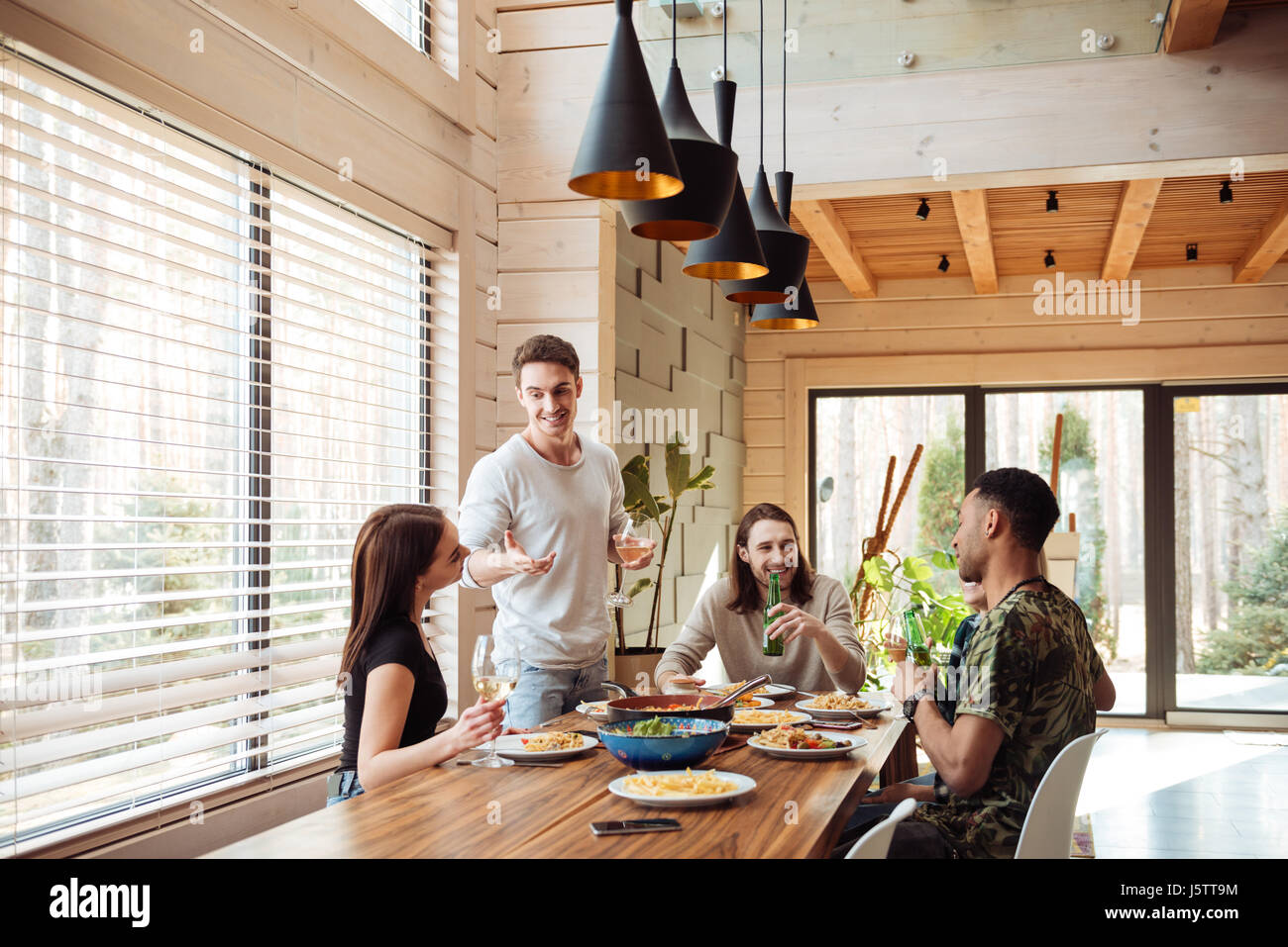 Group of happy young people eating and giving toasts at the table on ...