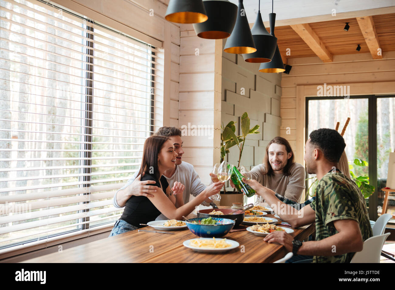 Group of cheerful young friends giving toasts and clinking glasses on ...