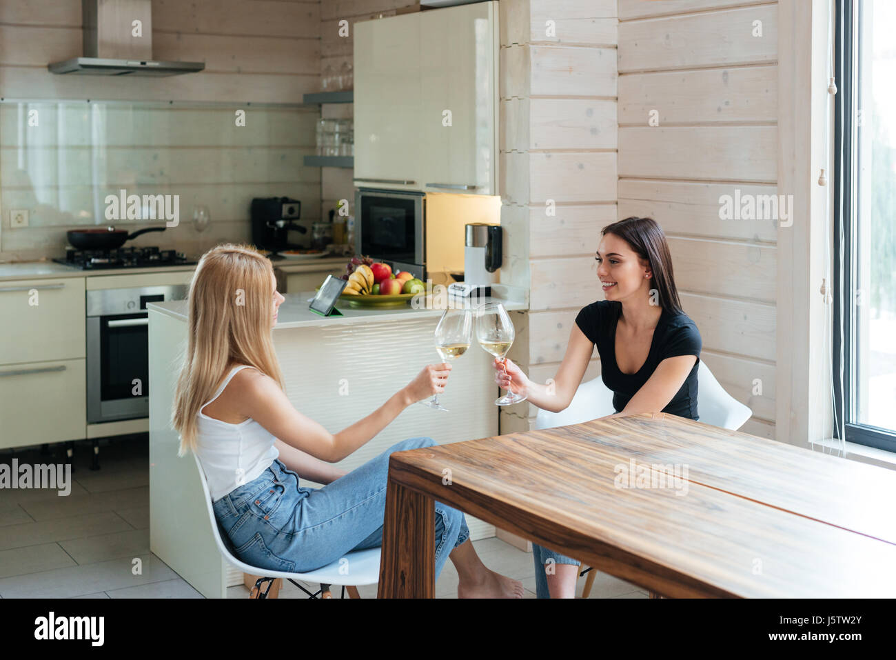 Side view of a Two friends sitting by the table in kitchen and drinking ...