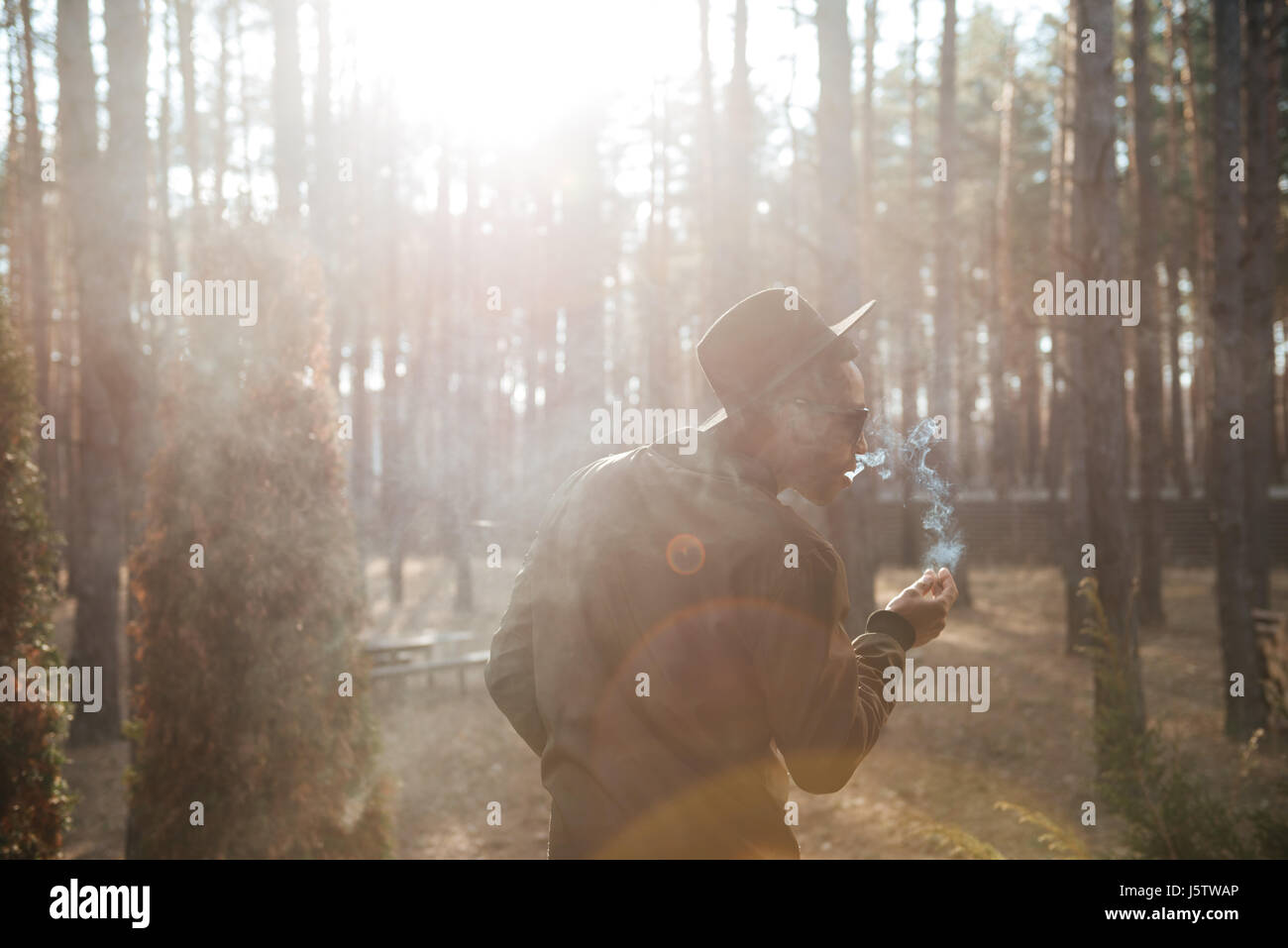Back view image of african man standing outdoors in the forest smoking ...