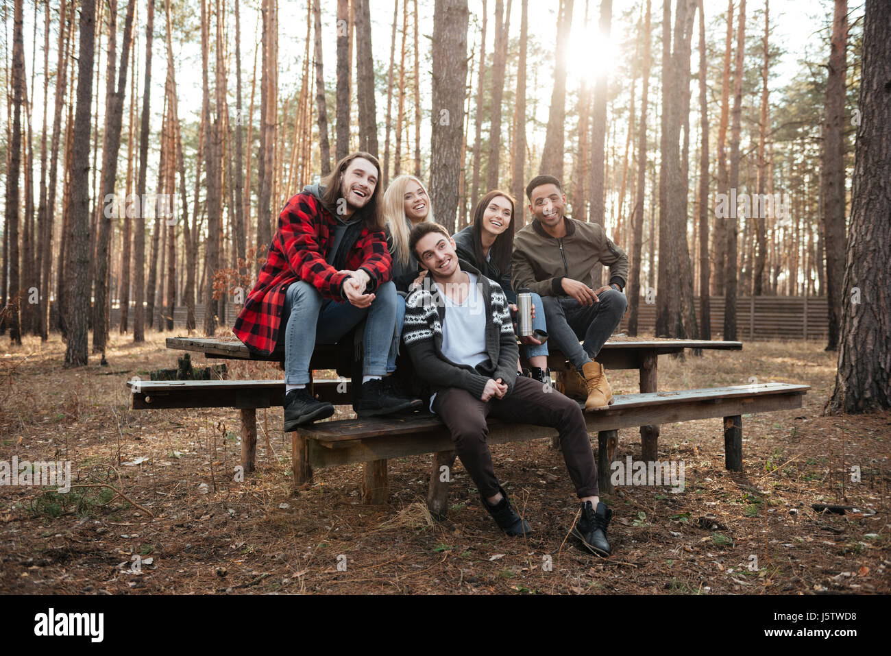 Image of happy group of friends sitting outdoors in the forest. Looking ...