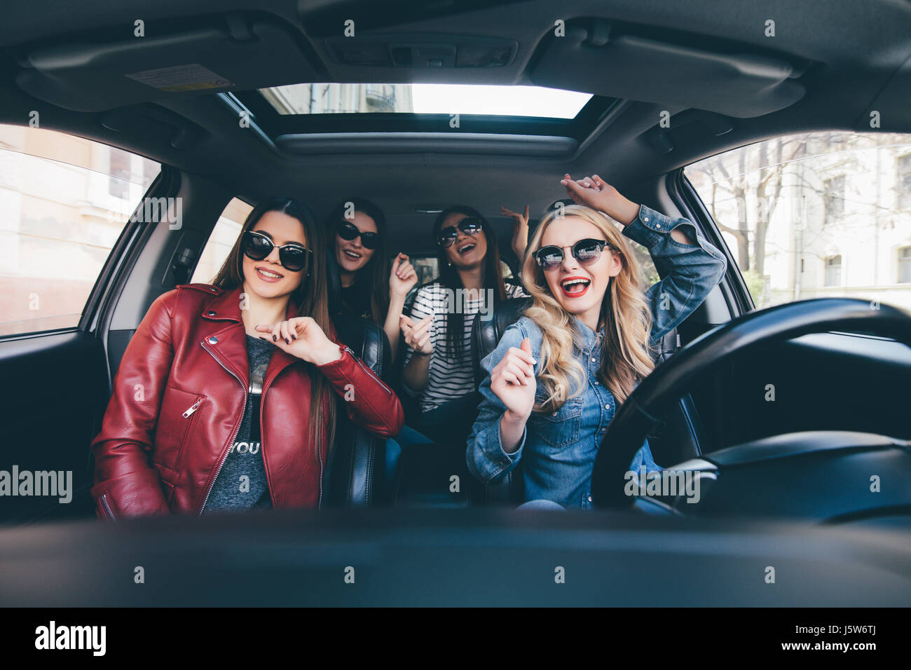 Driving together. Four beautiful young cheerful women looking at each ...