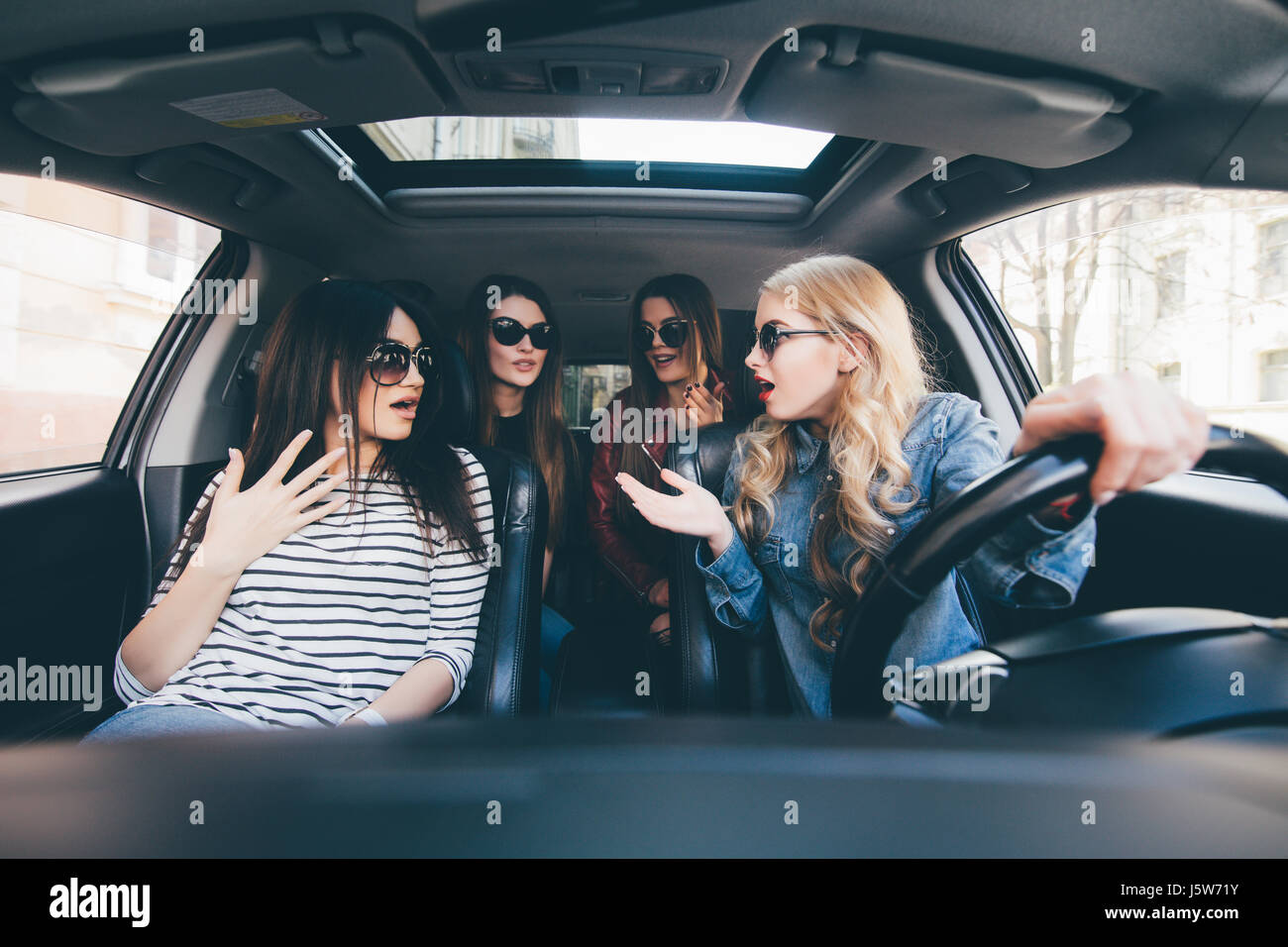 Driving together. Four beautiful young cheerful women looking at each ...