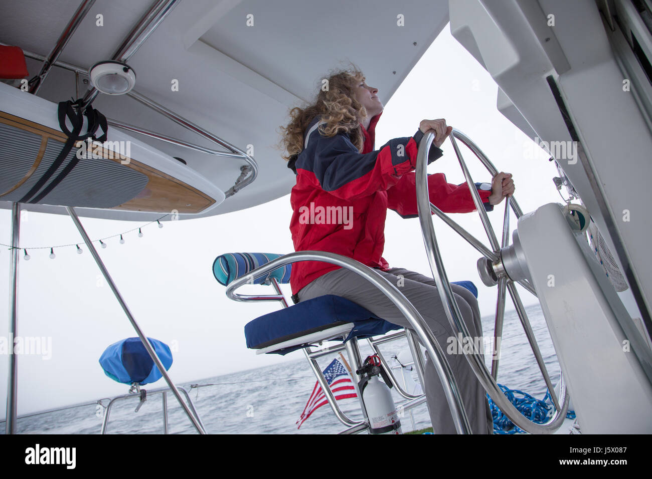 Young woman captains a sailing catamaran boat in foul weather rain and ...