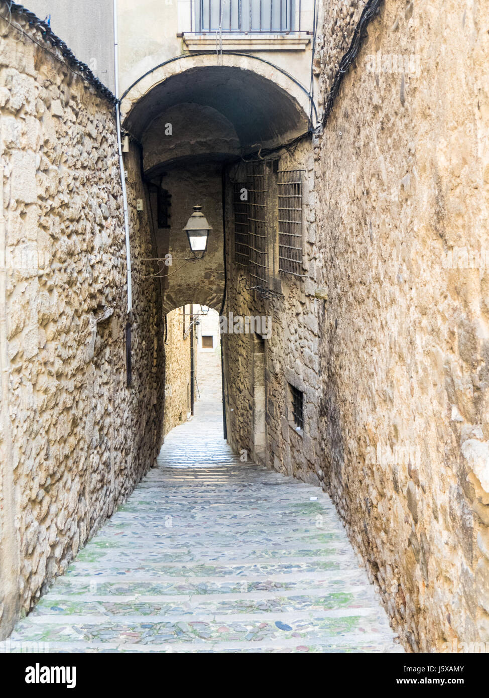 A narrow stone paved passageway between limestone walls, Girona, Spain ...