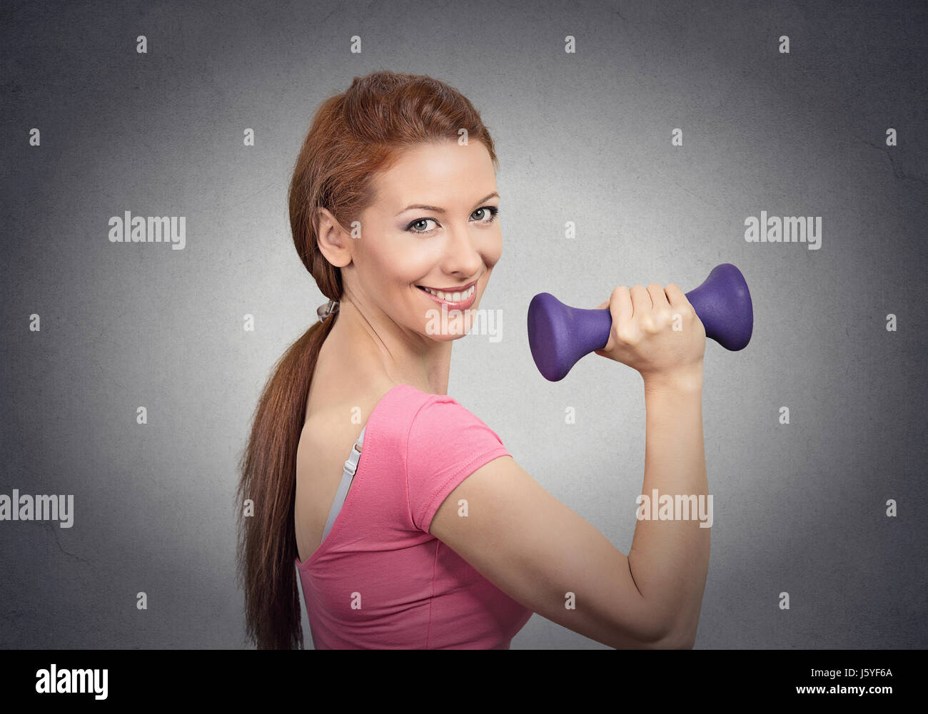 fit happy girl working out lifting dumbbell isolated on grey wall ...