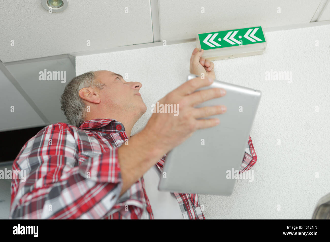 Man holding tablet, checking emergency exit sign Stock Photo - Alamy