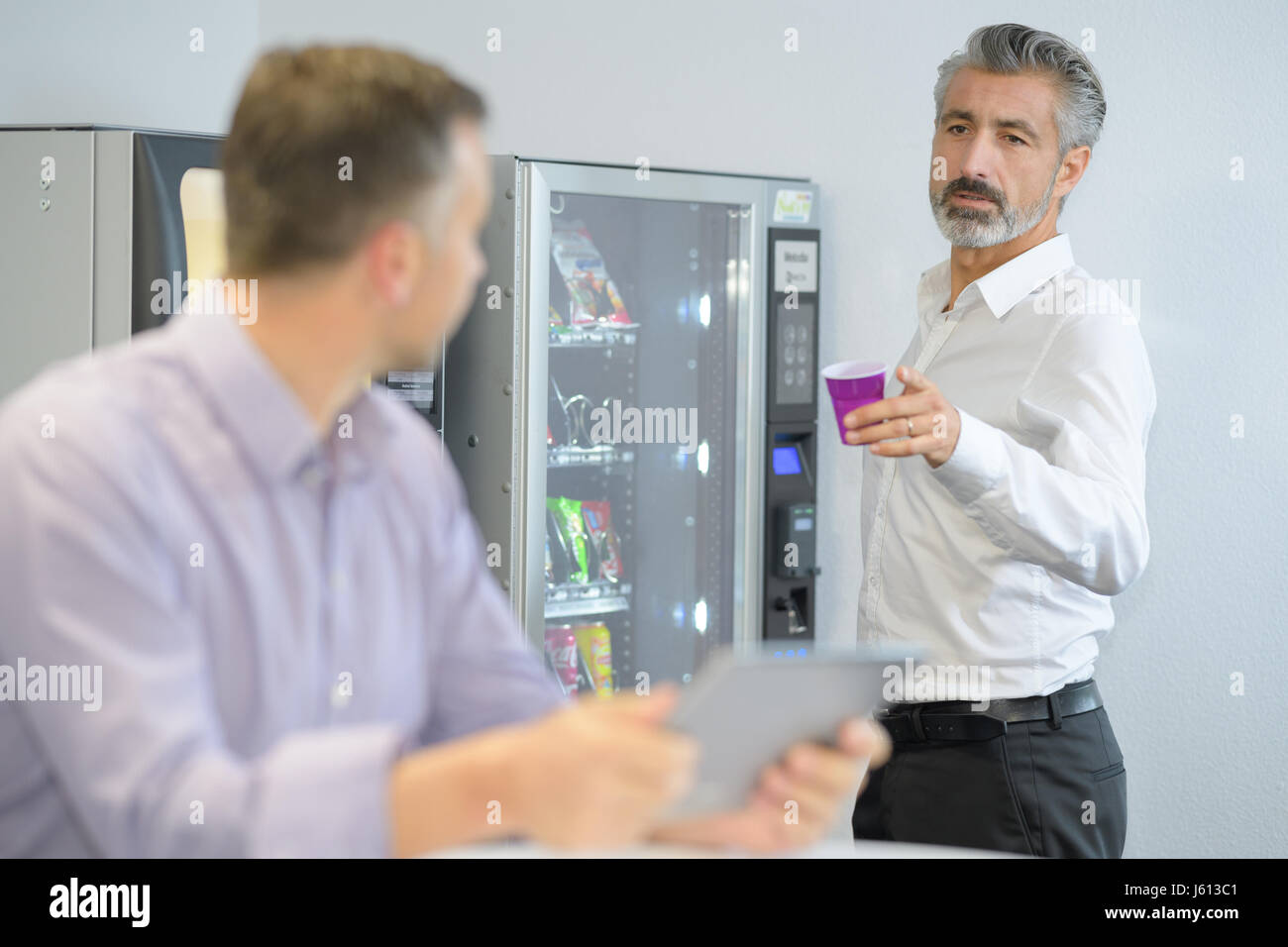Businessman offering coffee from vending machine Stock Photo - Alamy