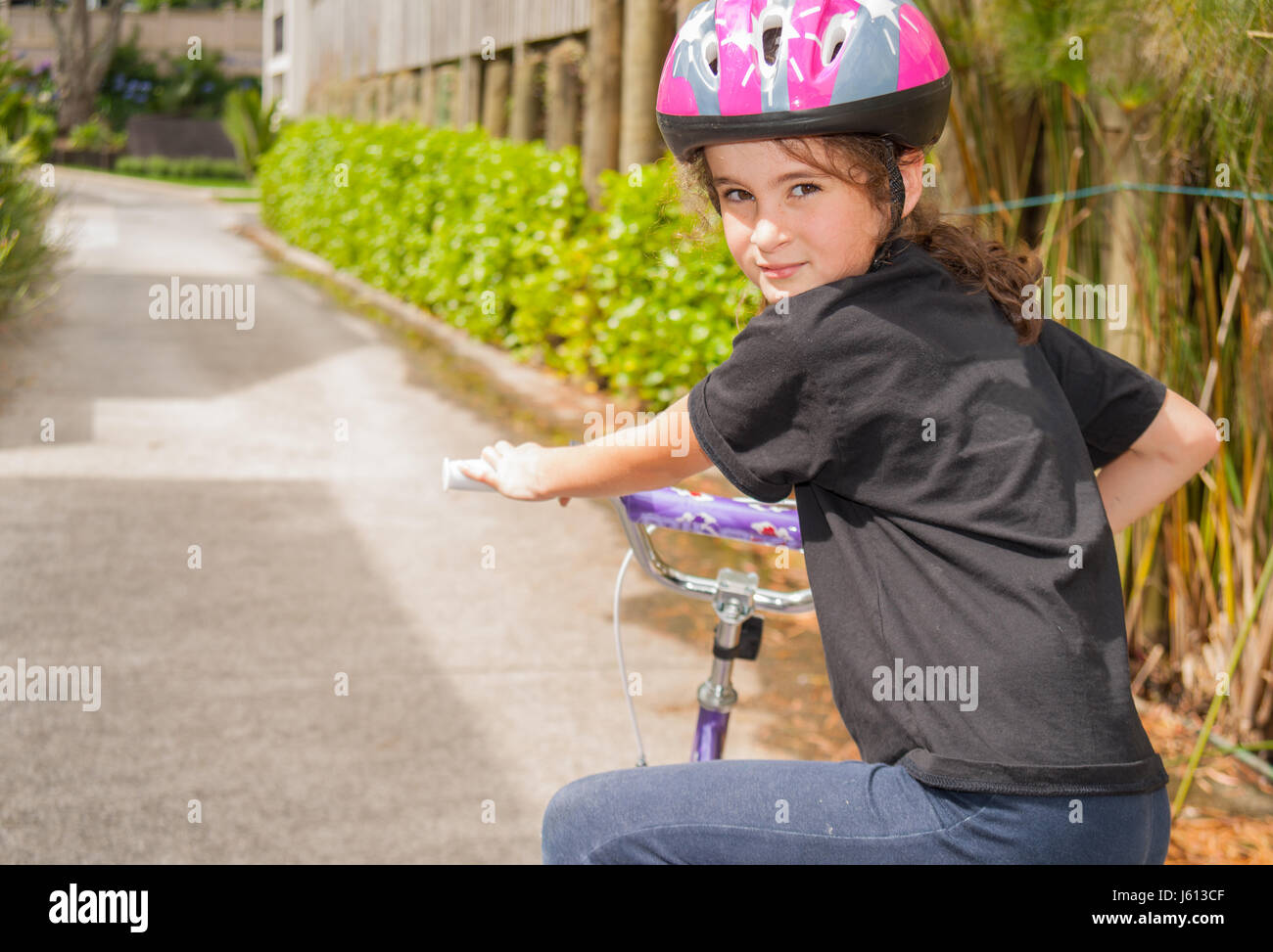 Young girl riding bicycle wearing helmet turns her head and looks back ...