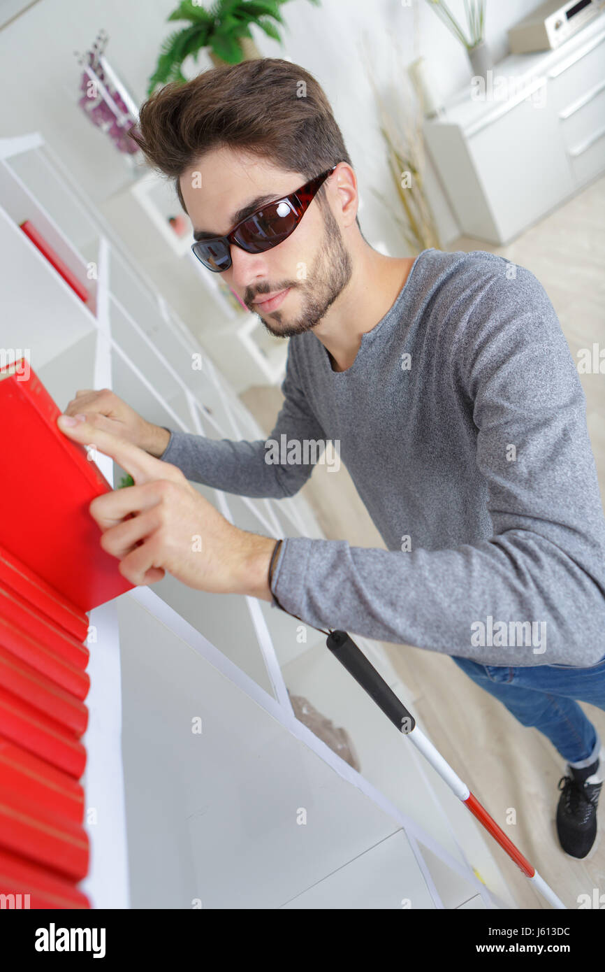 Young blind man feeling spine of book on shelf Stock Photo - Alamy