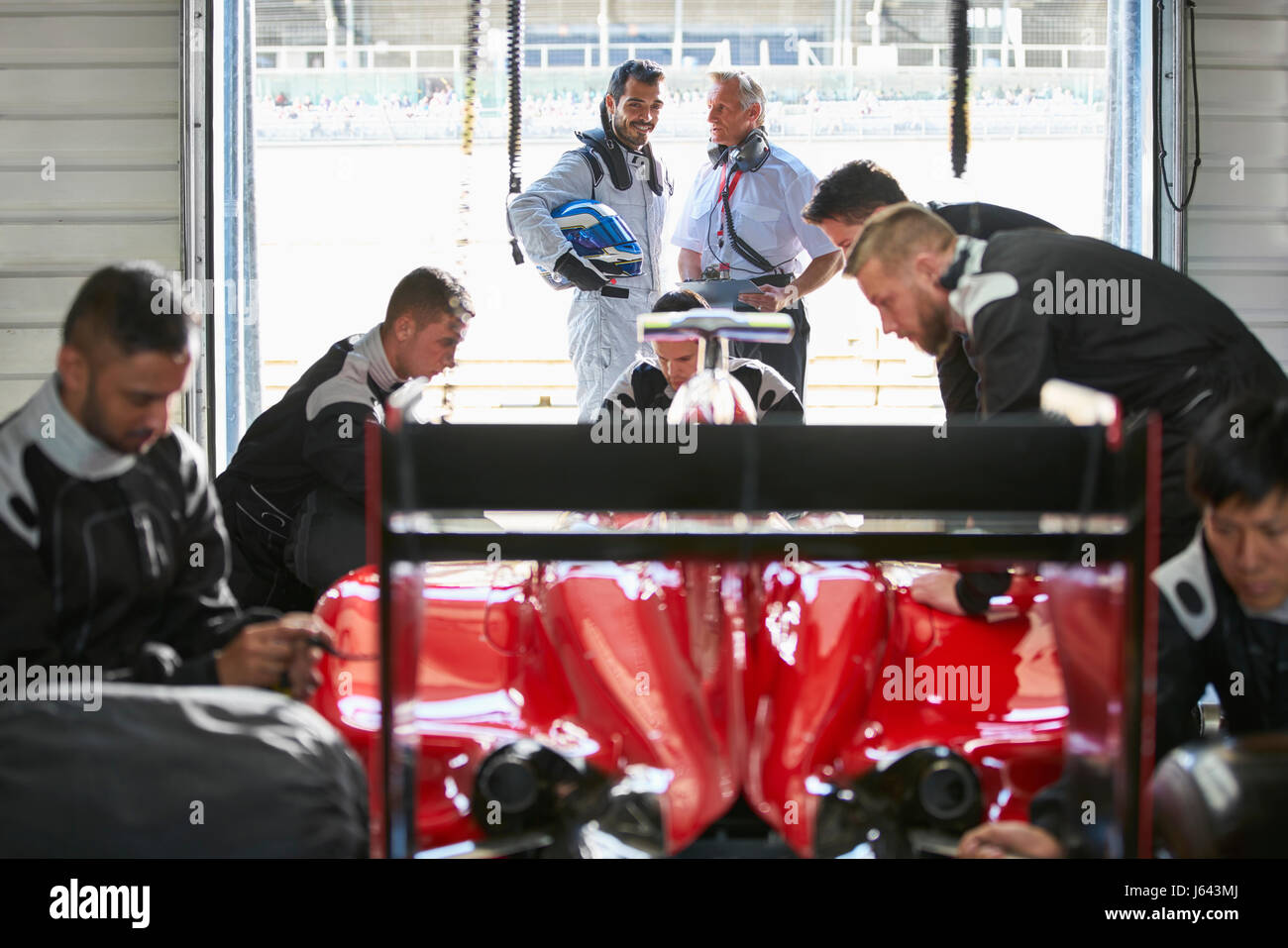 Formula one driver and manager talking behind pit crew working on race ...