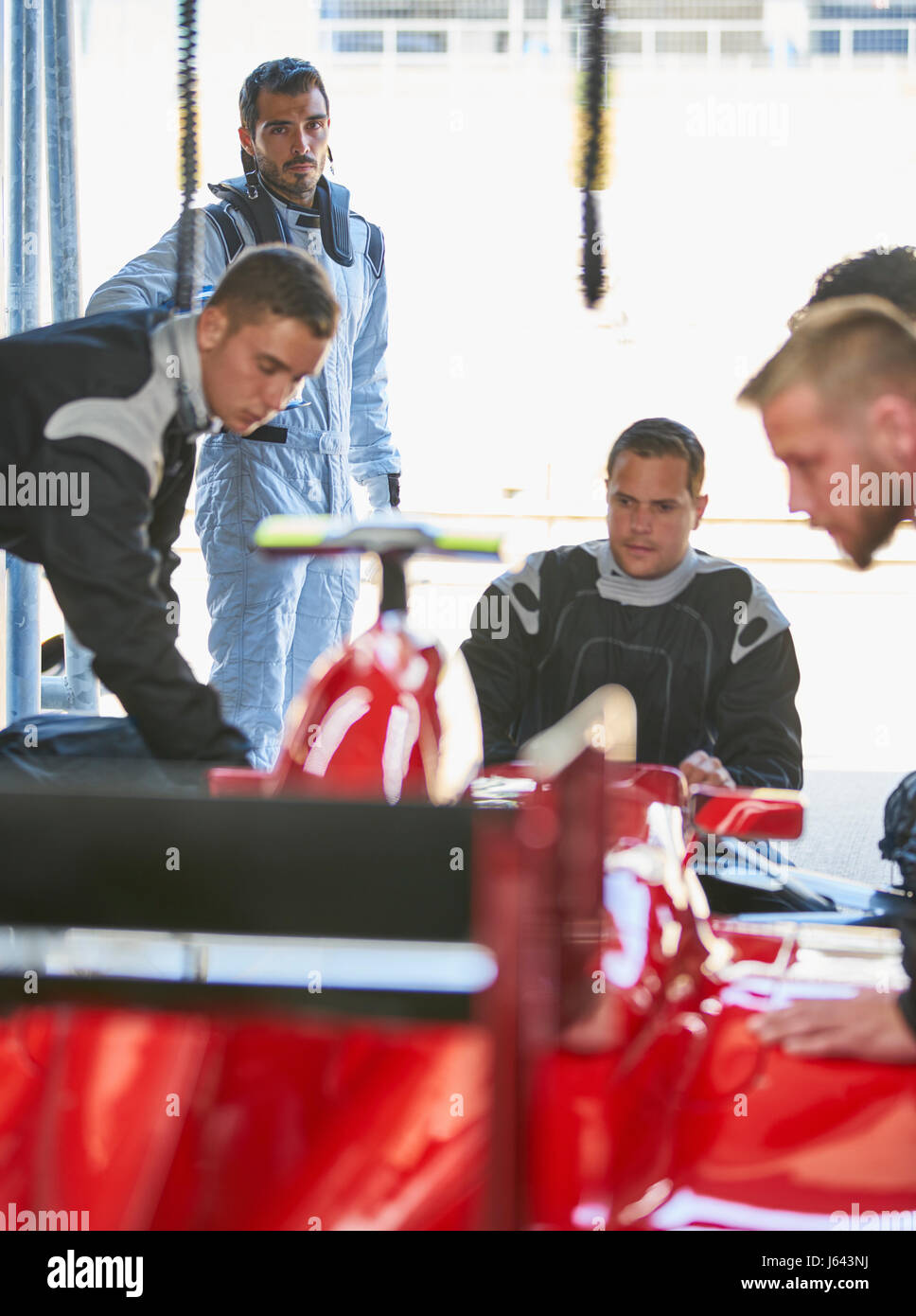 Formula one driver watching pit crew repairing race car in repair ...