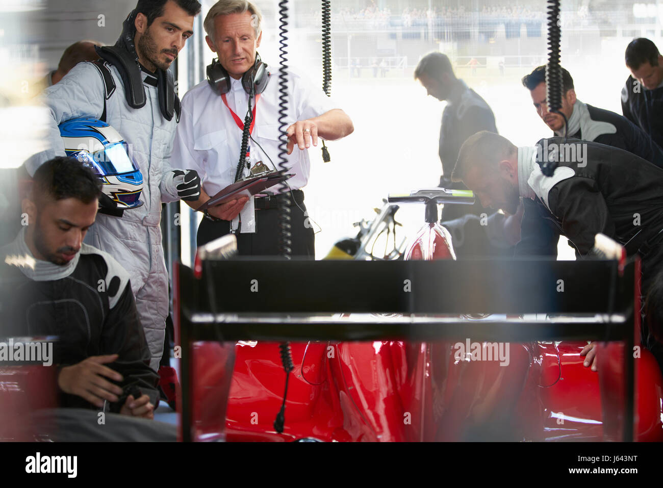 Manager and formula one driver watching pit crew working on race car in ...