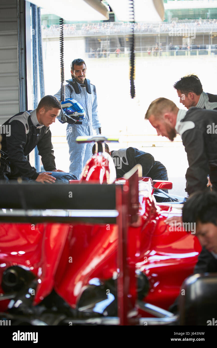 Formula one driver watching pit crew working on race car in repair ...