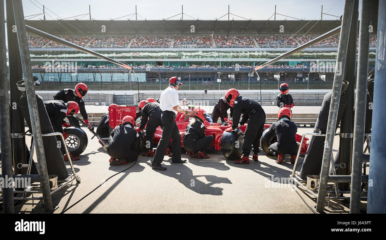 Manager and pit crew replacing tires on formula one race car in pit ...