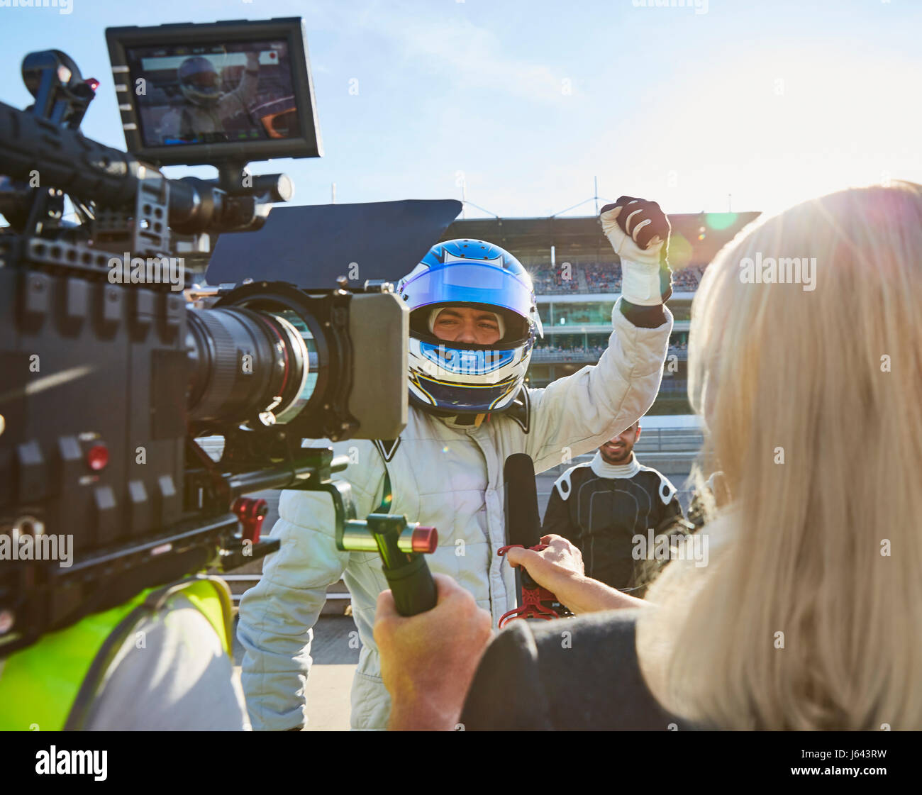 News reporter and cameraman interviewing formula one driver cheering ...
