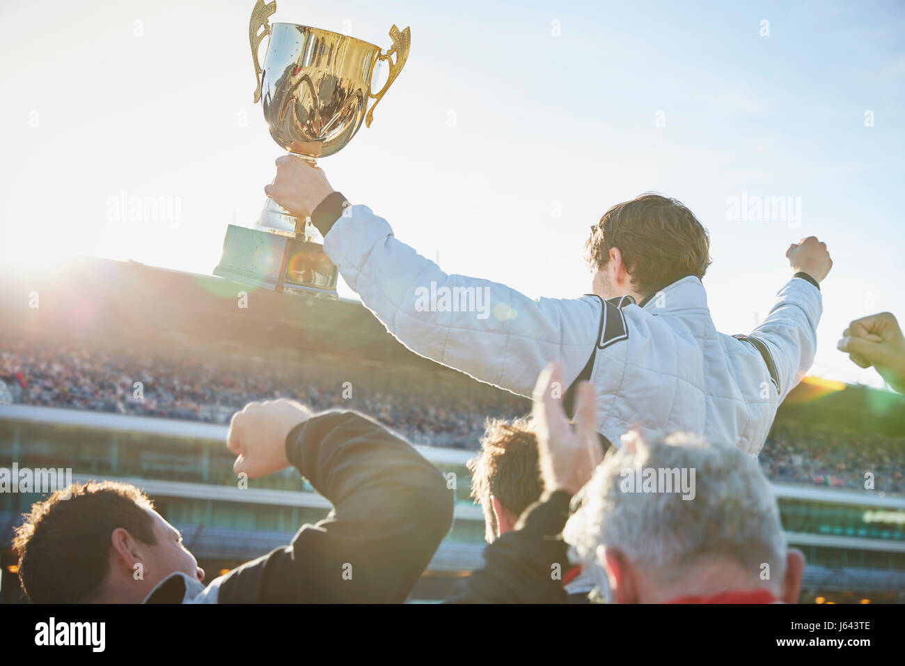 Formula one racing team carrying driver with trophy on shoulders ...