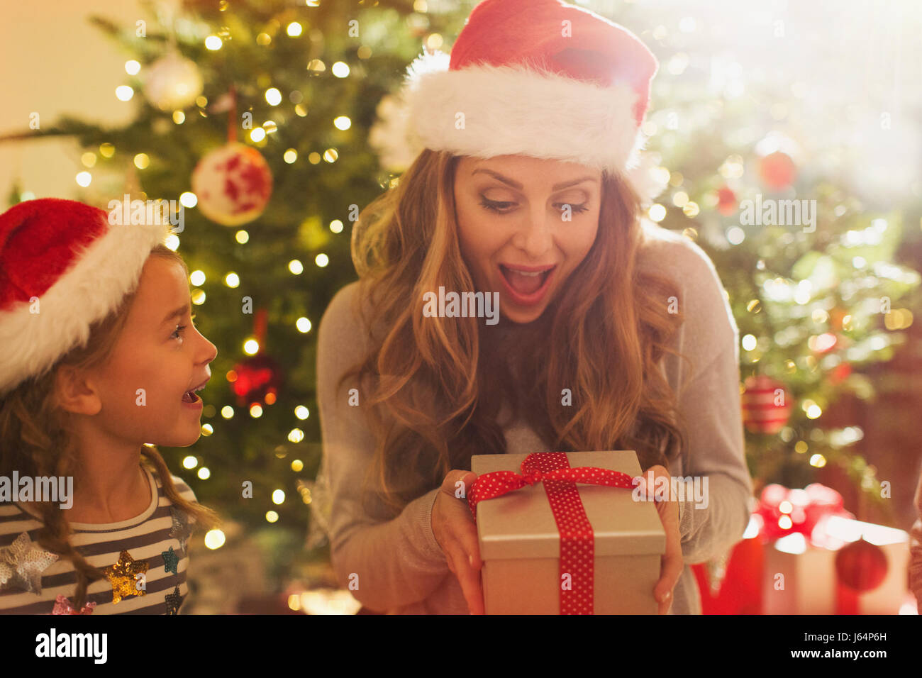 Surprised mother with Santa hat receiving Christmas gift from daughter ...