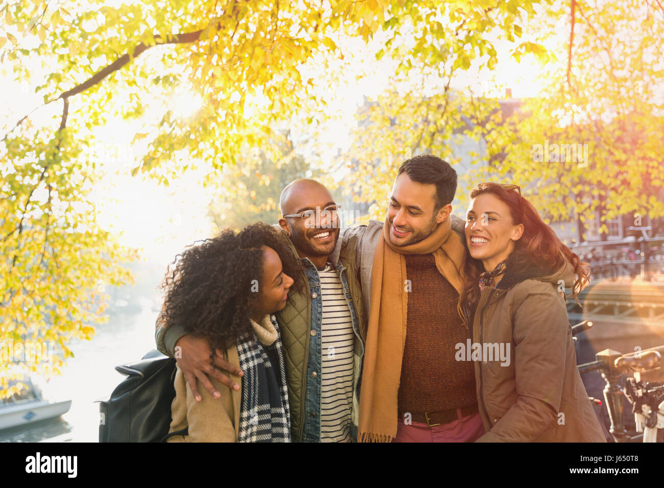 Smiling young friends hugging under sunny autumn tree Stock Photo - Alamy