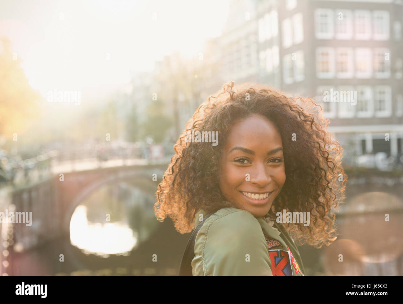 Portrait smiling young woman along urban canal, Amsterdam Stock Photo ...