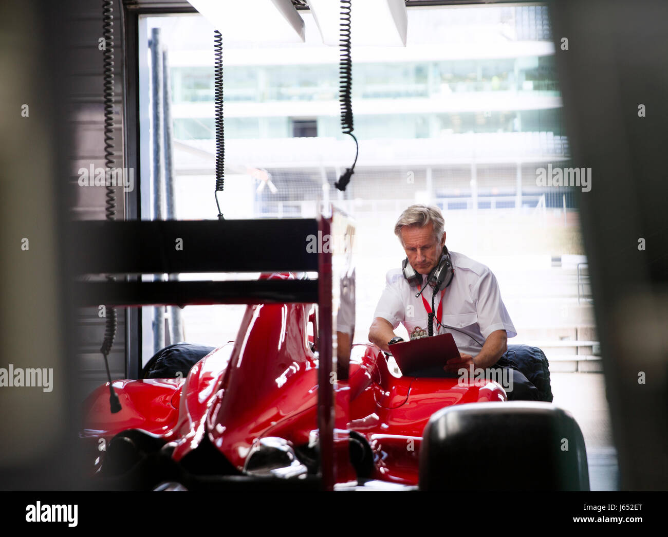Manager with clipboard examining formula one race car in repair garage ...