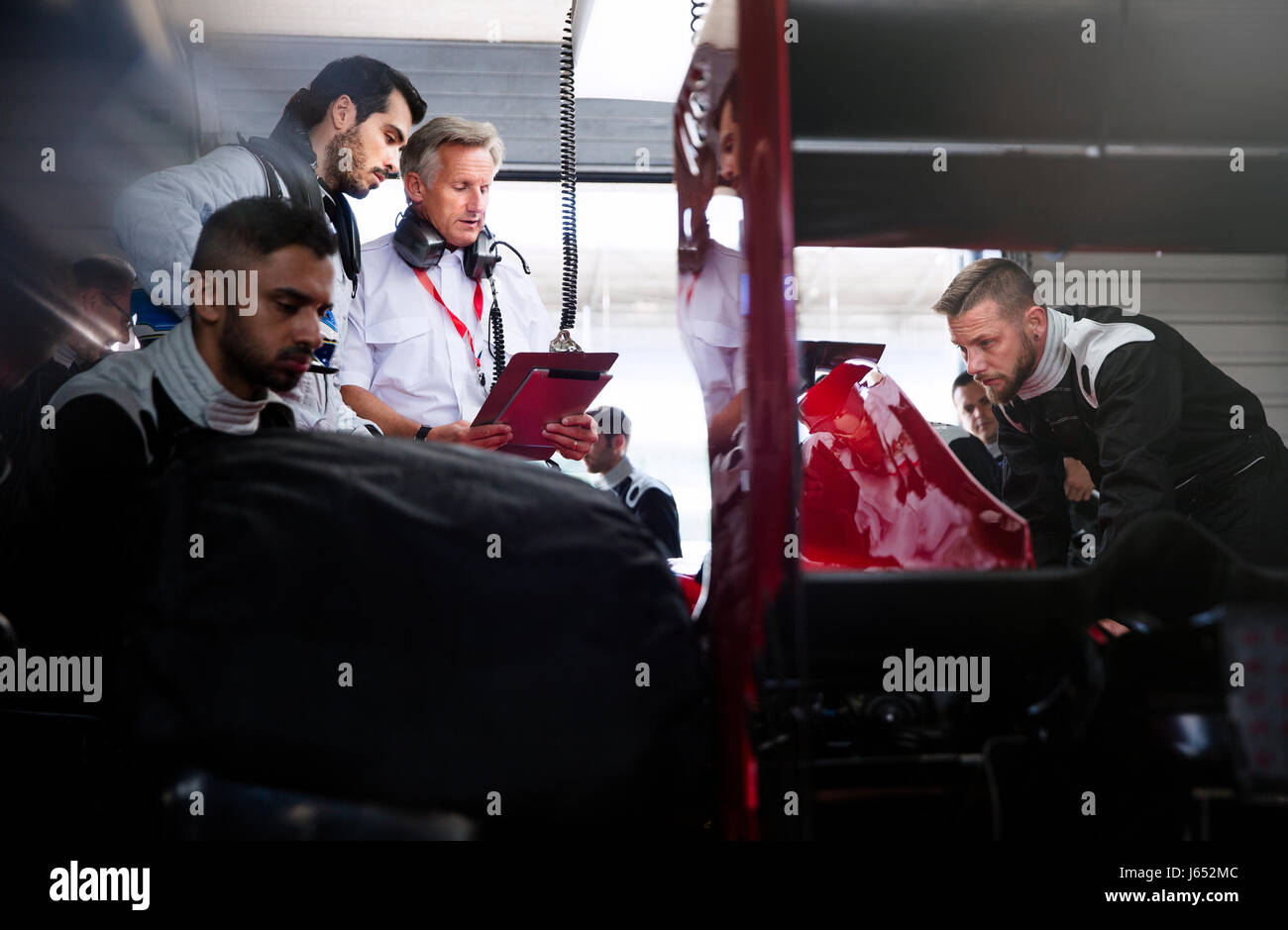 Manager and driver talking behind pit crew working on race car in ...