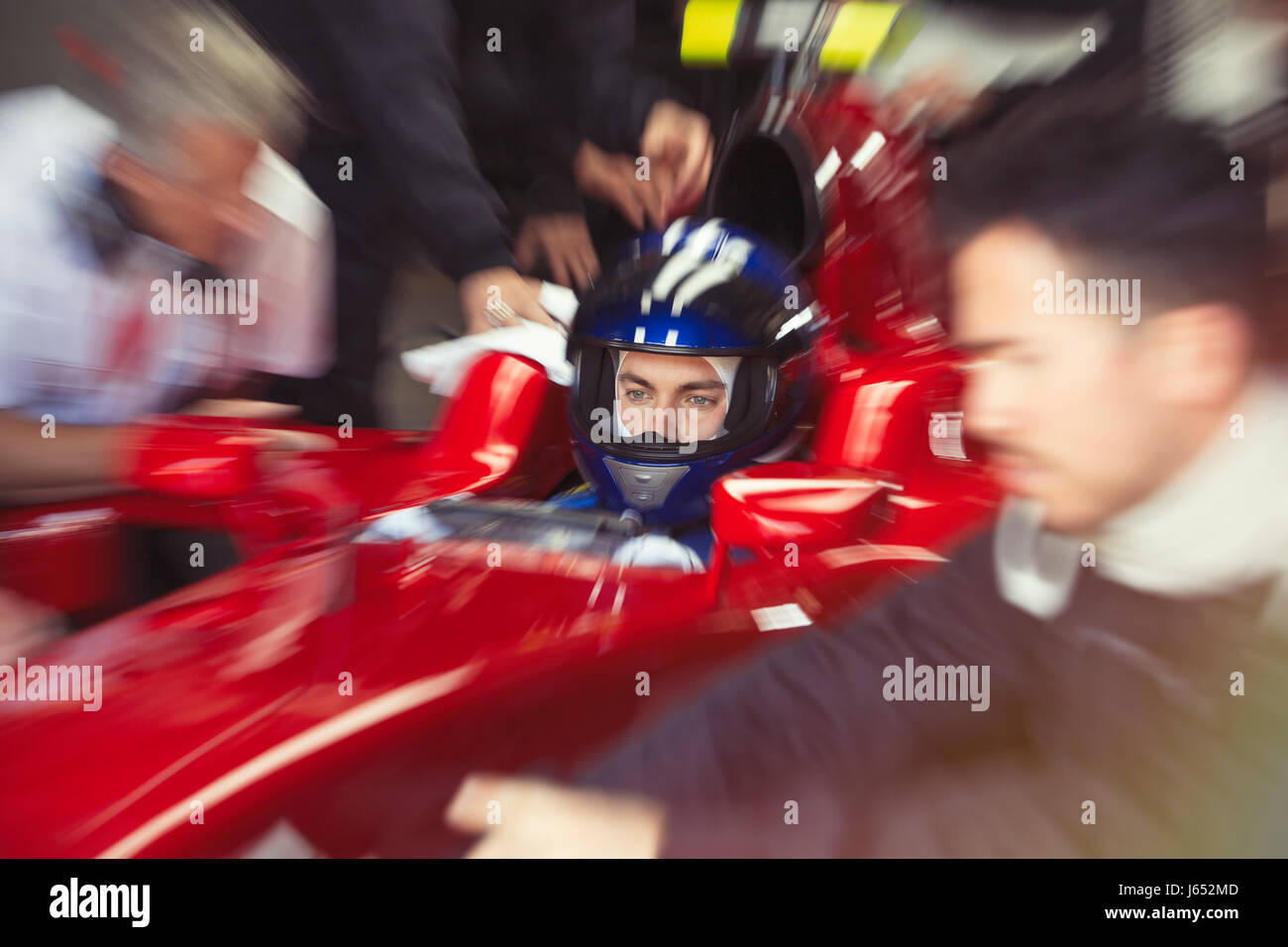 Pit crew preparing formula one race car around focused driver in repair ...