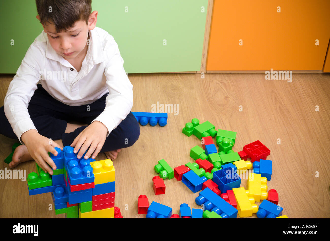 Little boy in a colorful room playing with construction toy blocks ...