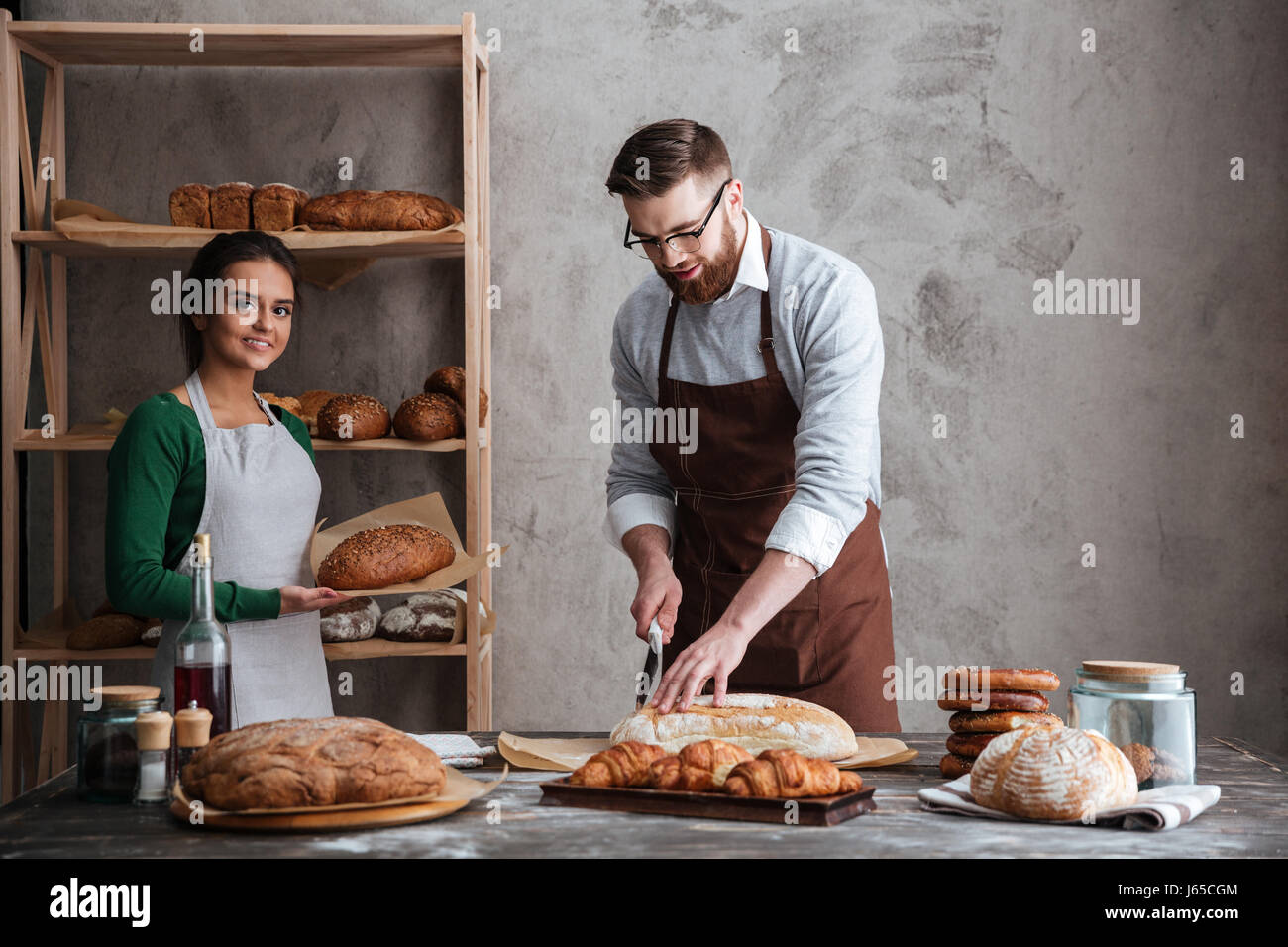 Image of happy loving couple bakers. Man cut the bread. Woman looking ...