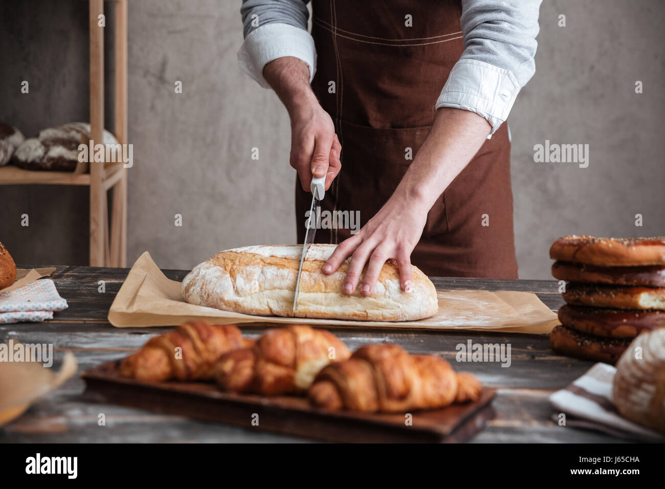 Cropped image of young man baker standing at bakery cut the bread Stock ...