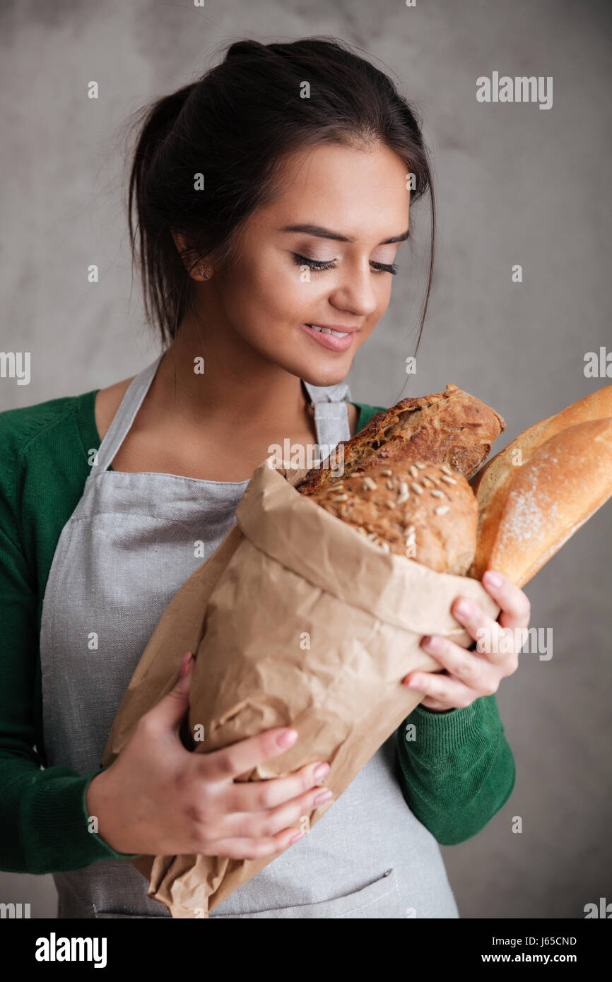 Picture of young happy lady baker standing and holding bread. Looking ...
