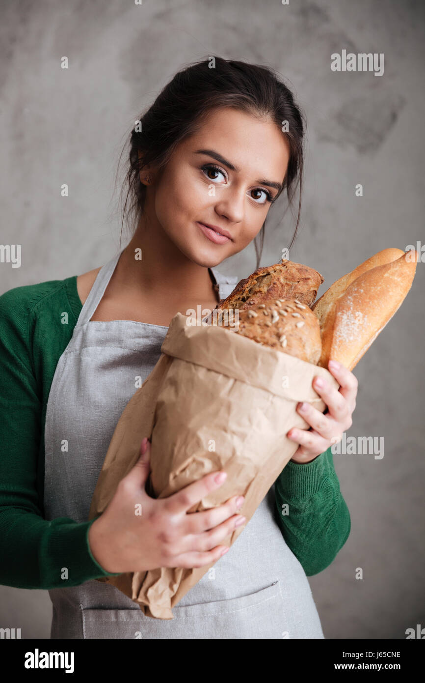 Picture of young happy lady baker standing and holding bread. Looking ...