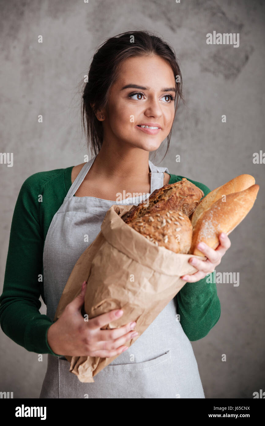 Picture of young smiling lady baker standing and holding bread. Looking ...