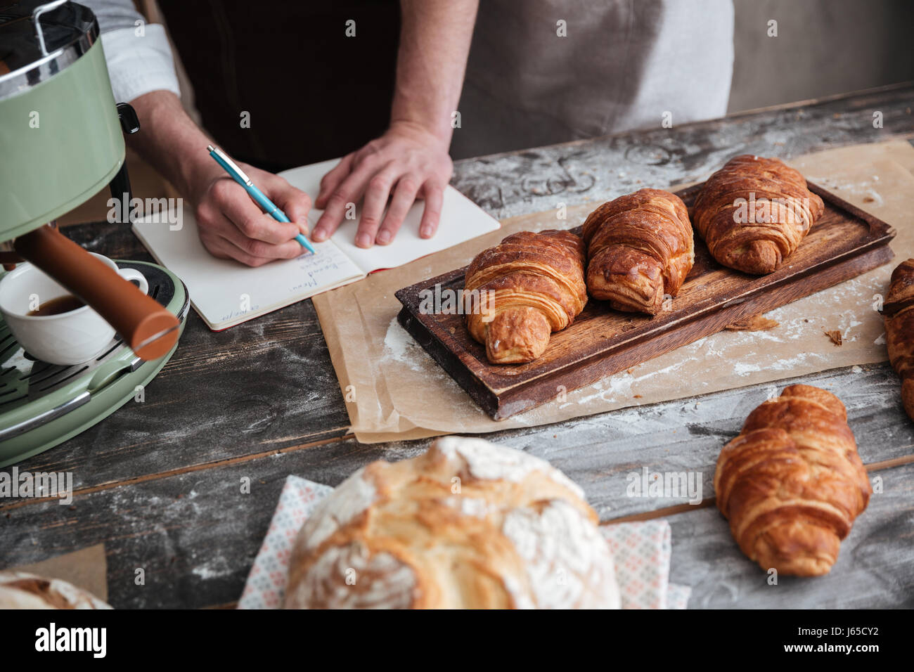 Cropped picture of man baker writing notes at notebook standing at ...