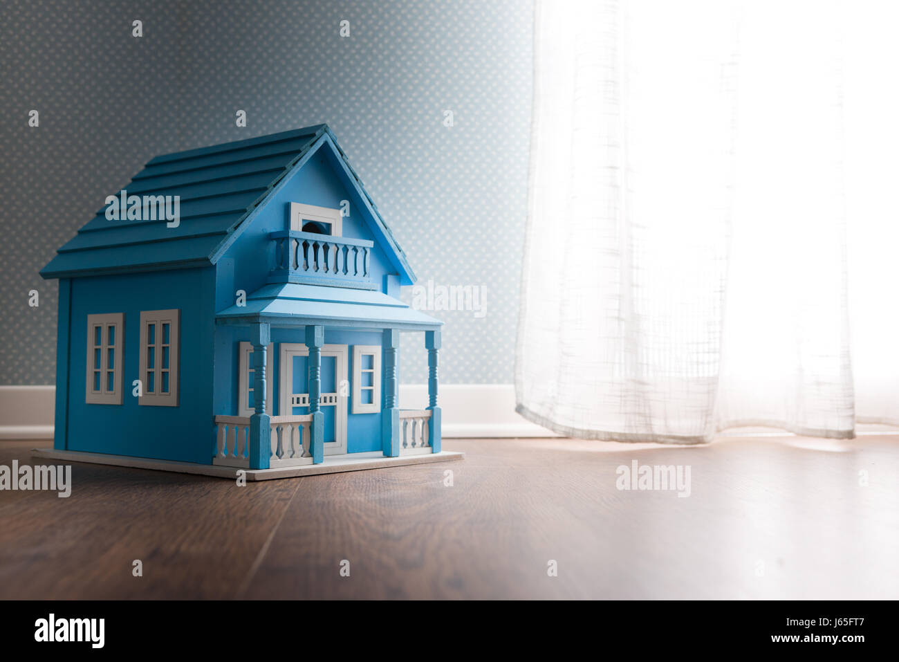 Blue wooden model house next to a window with curtain on wooden floor ...