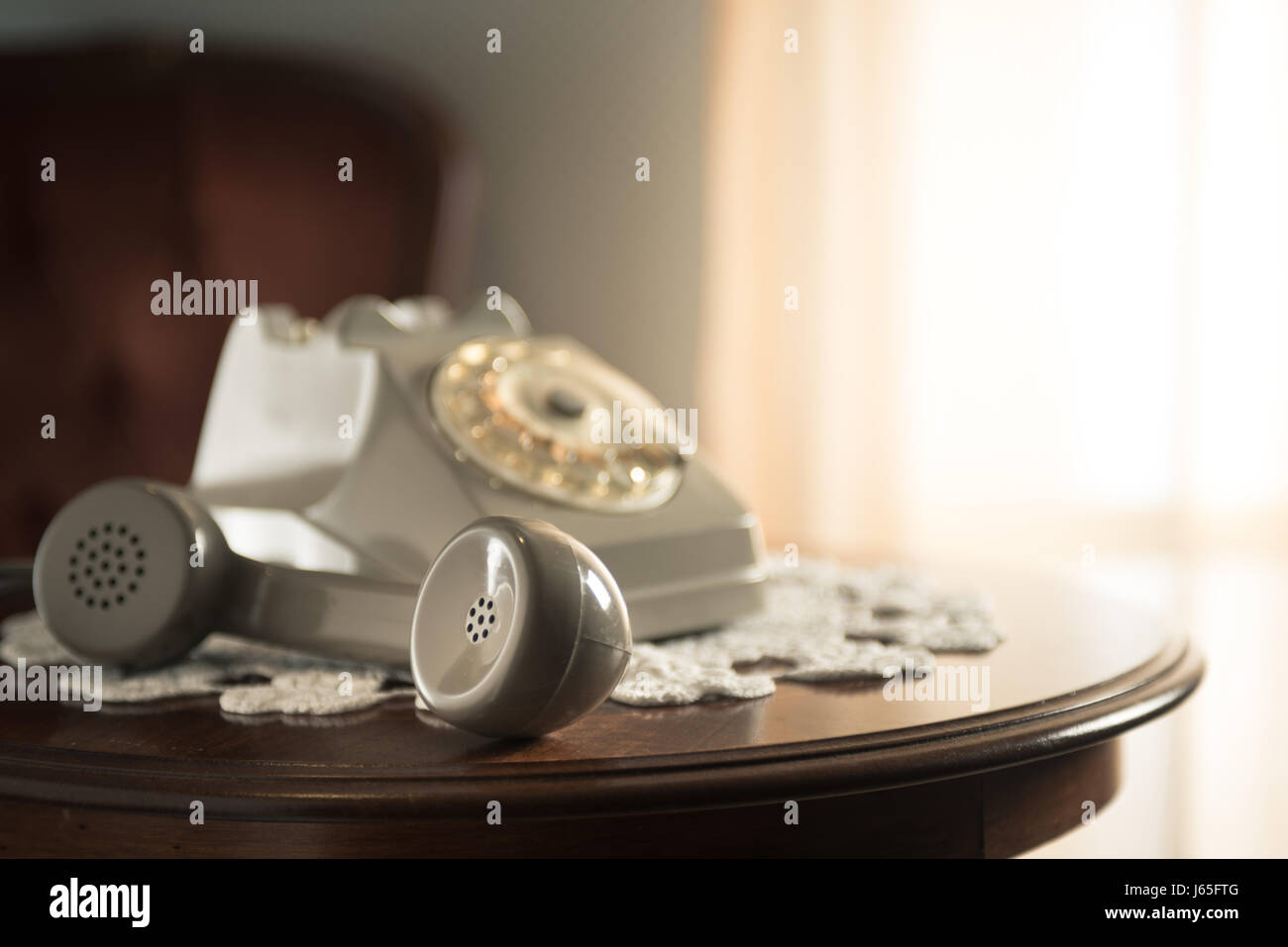 Vintage telephone on doily and round wooden table with handset on hold ...