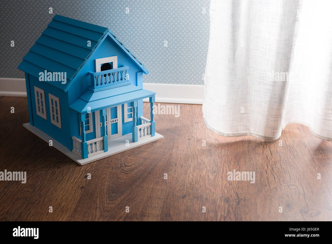 Blue wooden model house next to a window with curtain on wooden floor ...