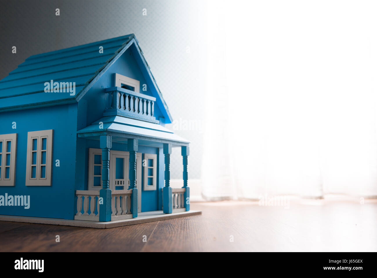 Blue wooden model house next to a window with curtain on wooden floor ...