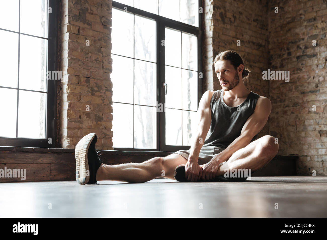 Portrait of a young sportsman doing stretching exercises while sitting ...