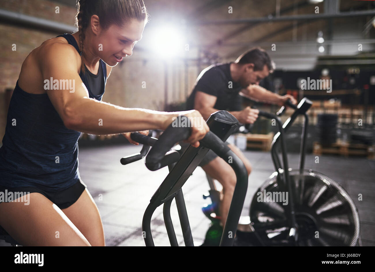 Two young sportsmen sitting on cycling machines and working out in ...
