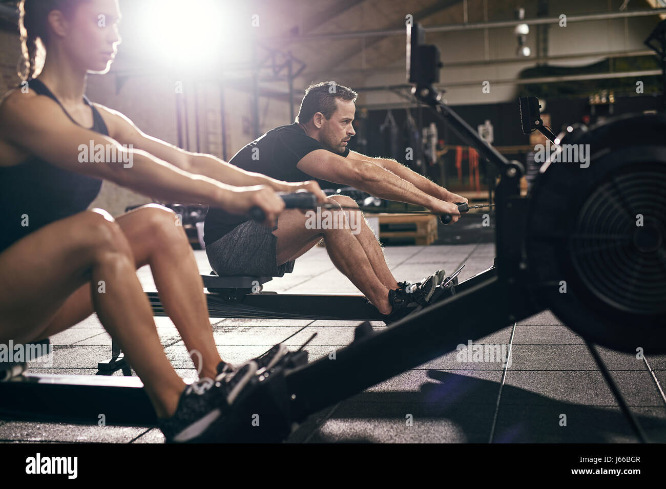 Side view of man and woman doing exercises with rowing machine at gym ...