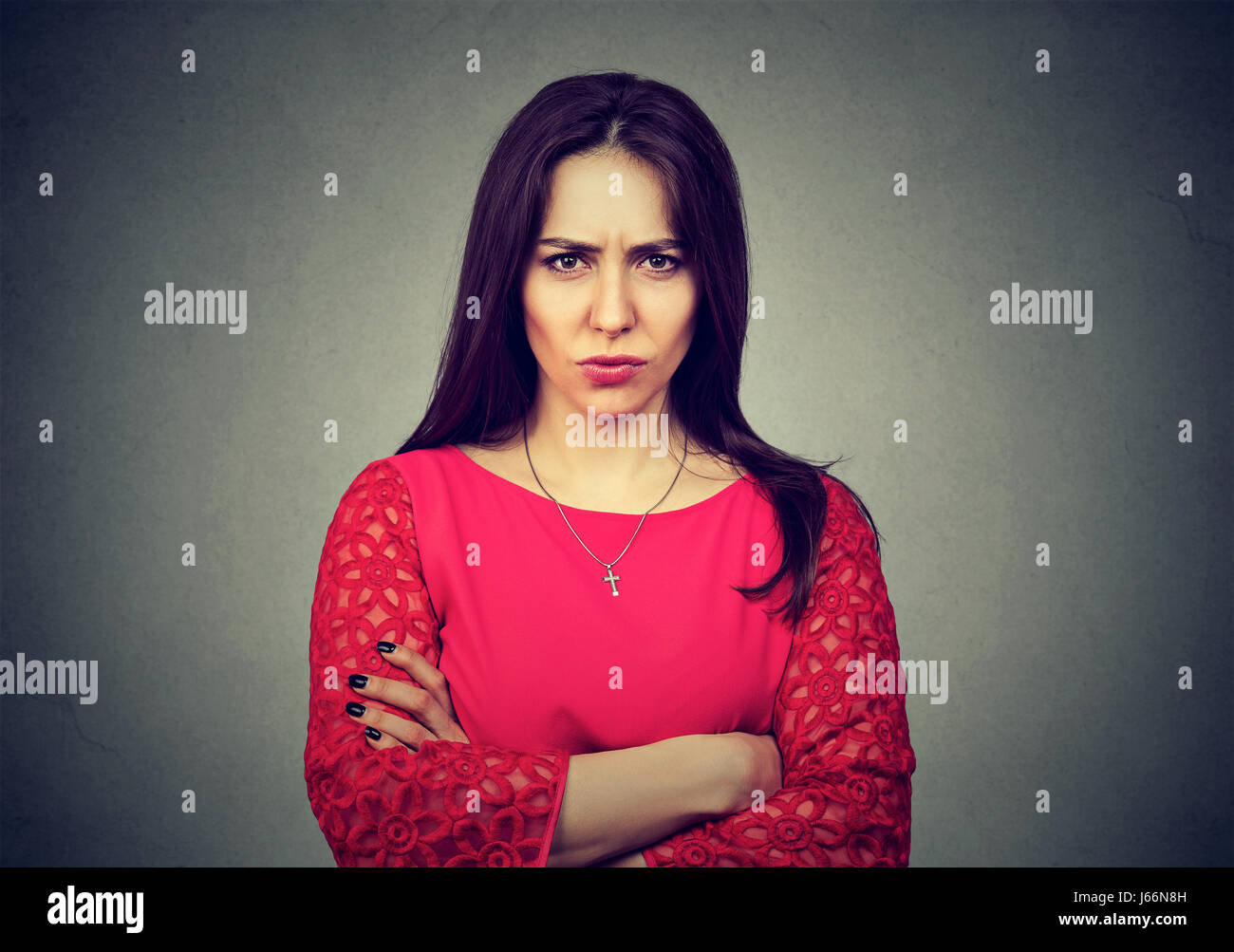 Portrait of angry woman standing with arms folded on gray background ...