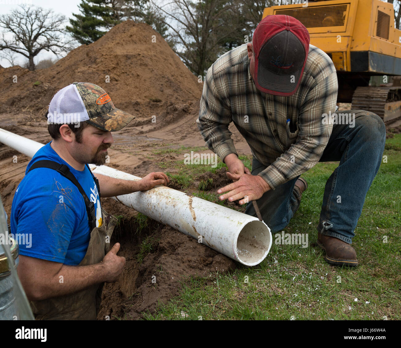 Two farmers file down the end of an irrigation pipe that is being ...