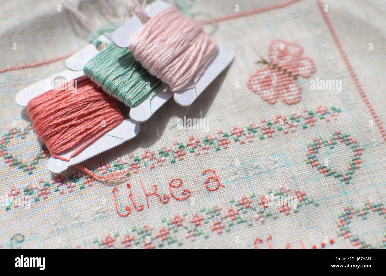 Cross-stitch embroidery on linen and three bobbins of thread. Sampler ...