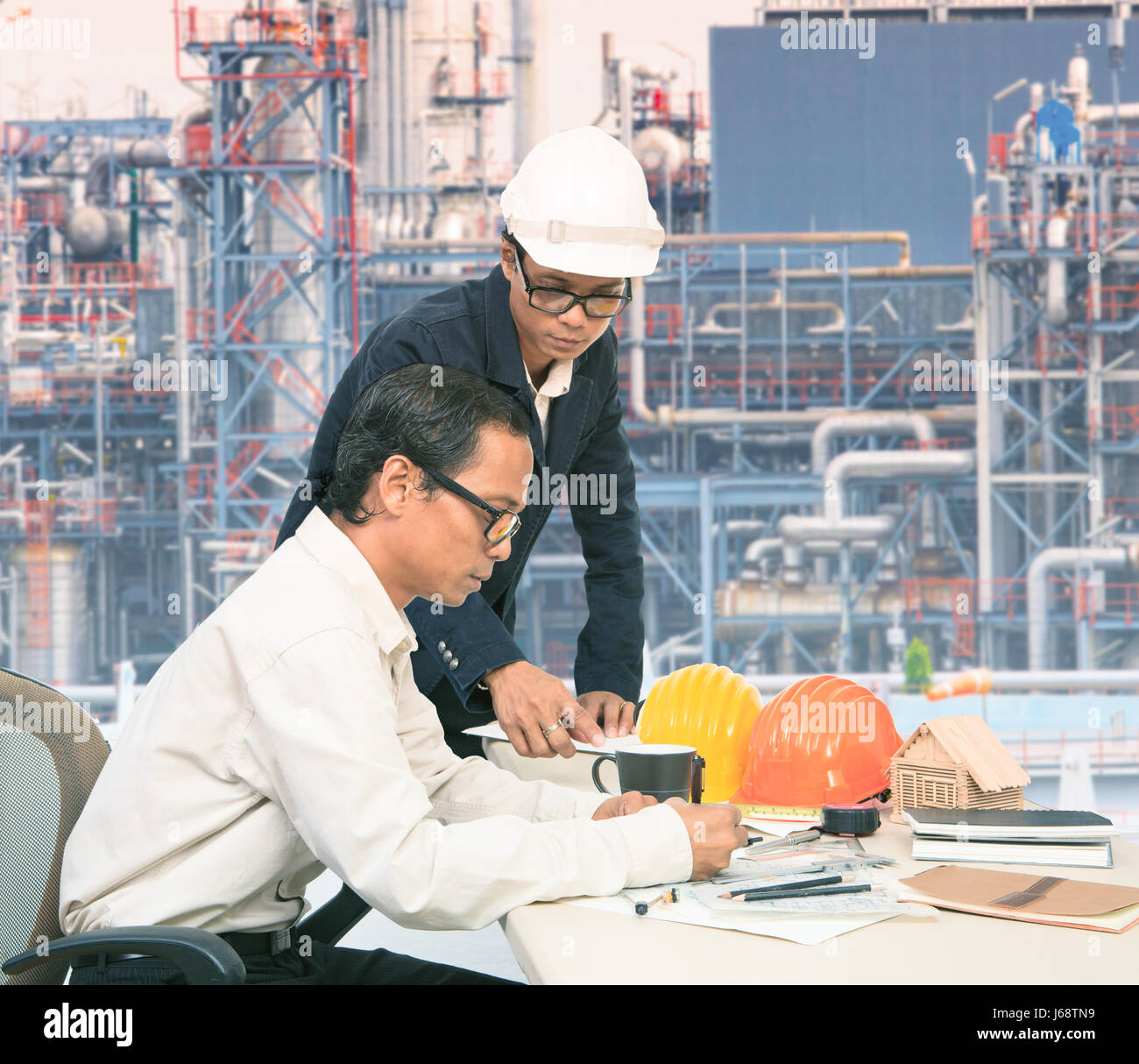 two engineer working on table against exterior of oil refinery plant ...