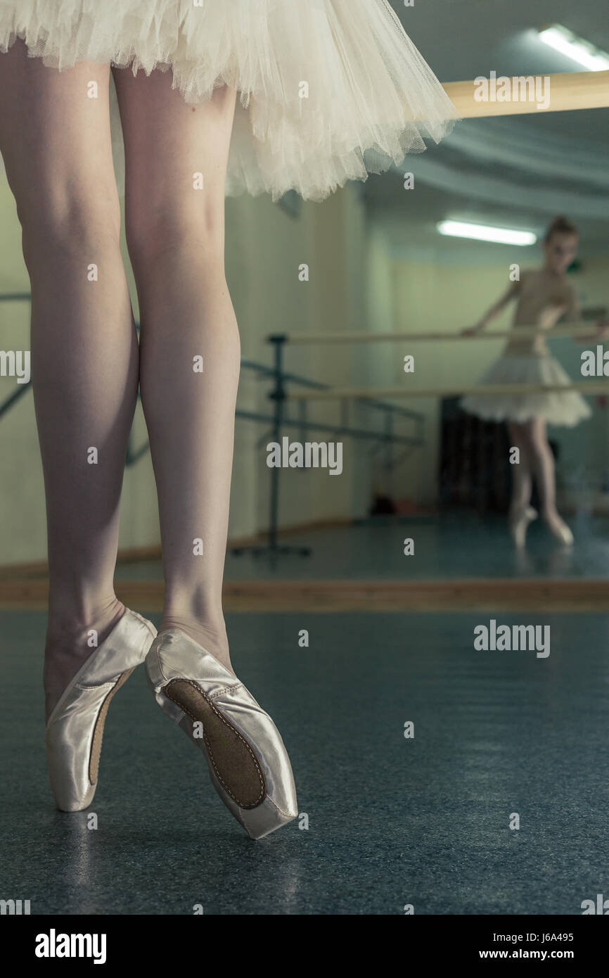 Ballerina in pointe shoes and tutu standing on toes at the bench ...