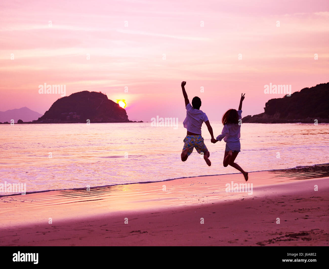 young asian couple cheering and rejoicing on beach as the sun rising ...