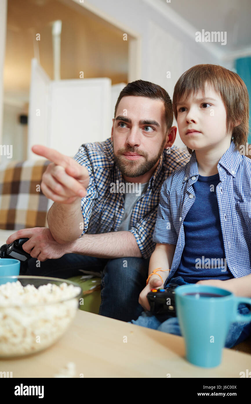 Father pointing at tv screen while gaming with his son at leisure Stock ...