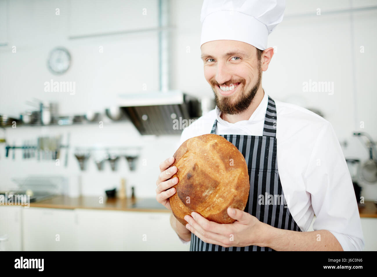 Smiling baker with crusty loaf of bread looking at camera Stock Photo ...